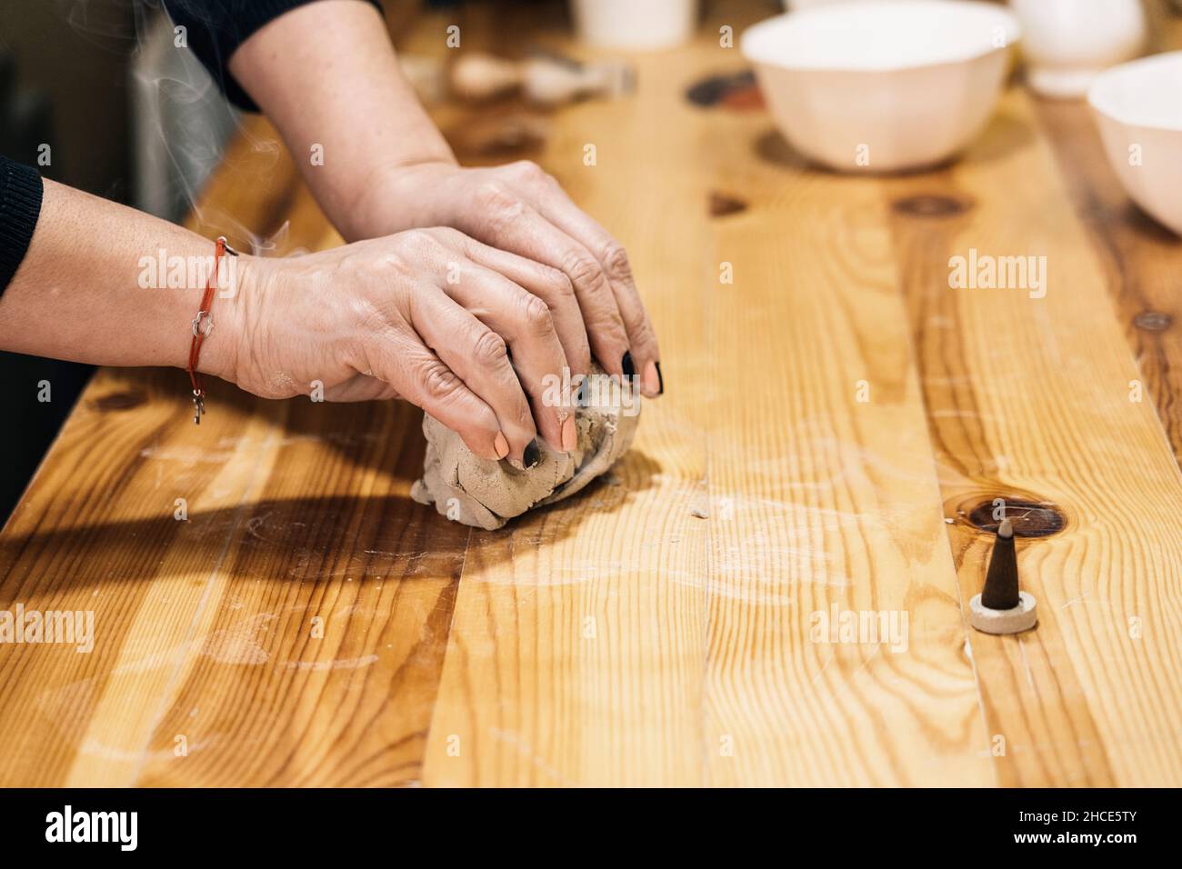 Crop unrecognizable female artisan rolling piece of clay on wooden ...
