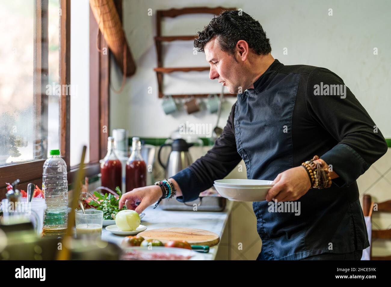 Side view of handsome male chef in black uniform holding plates while ...