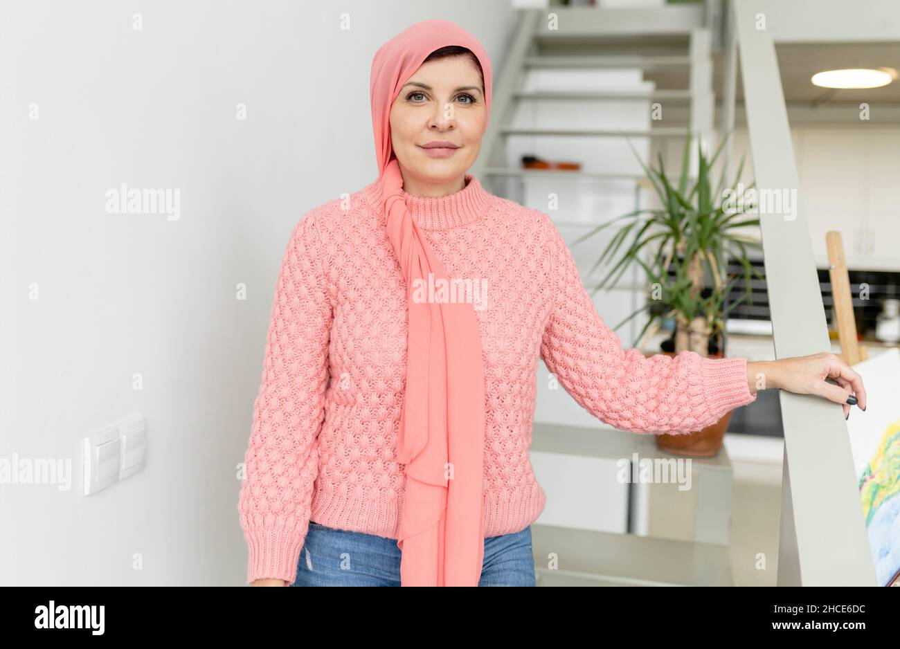 Thoughtful female wit cancer in sweater and pink headscarf looking out ...