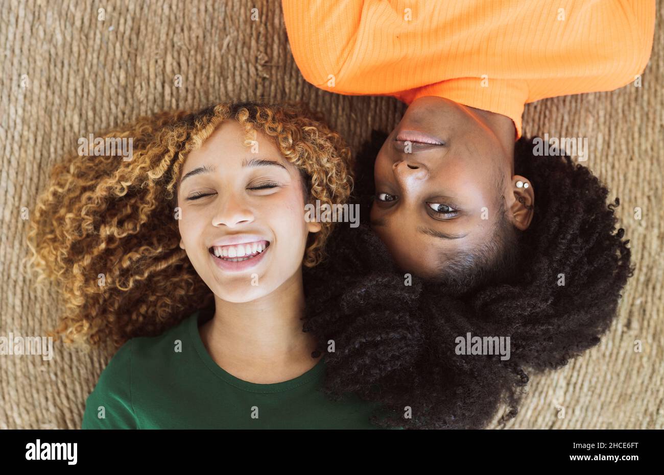 Top view of smiling multiracial women friends lying on wicker carpet on ...