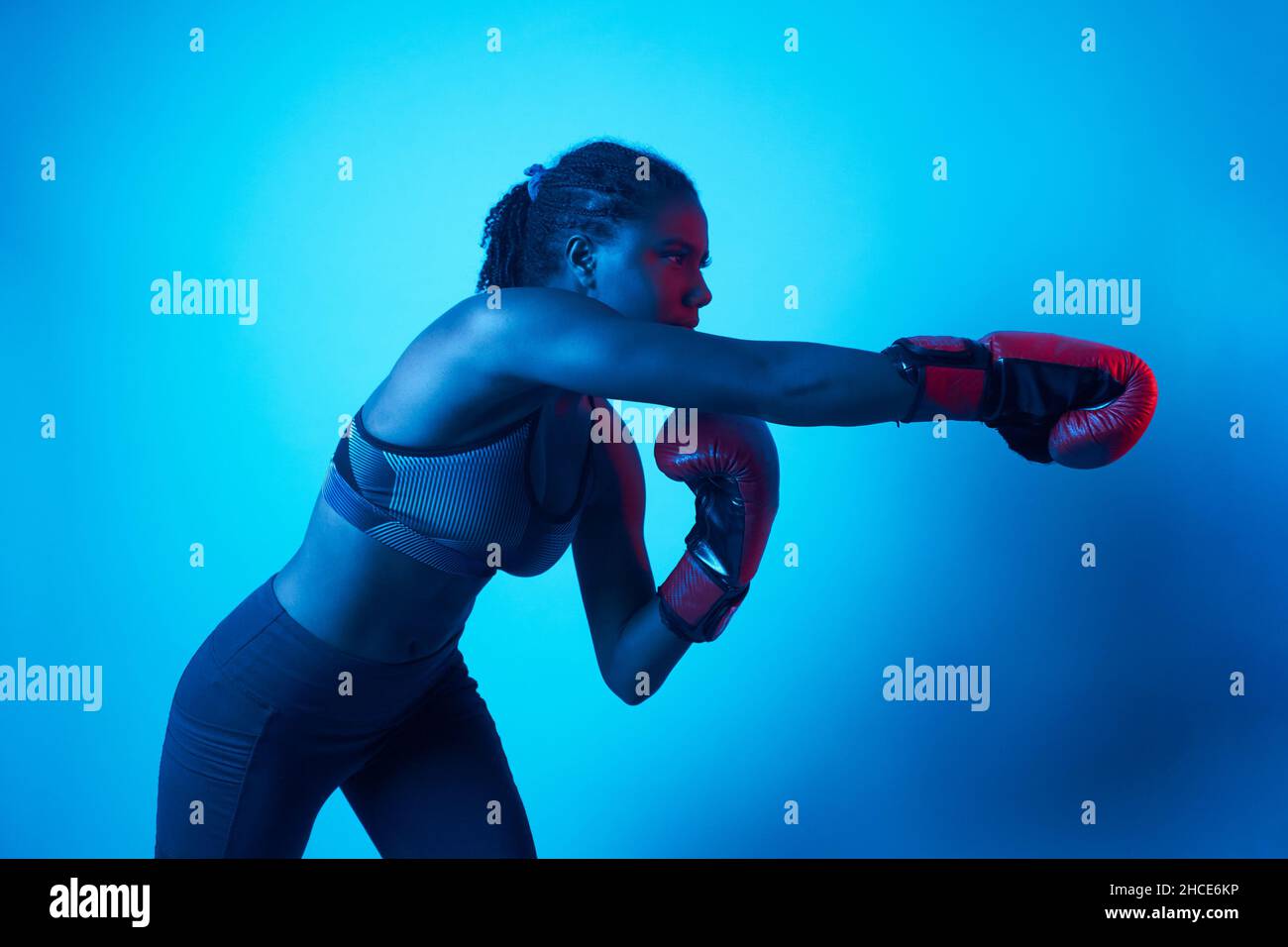 Side view of black female fighter in boxing gloves standing in blue ...