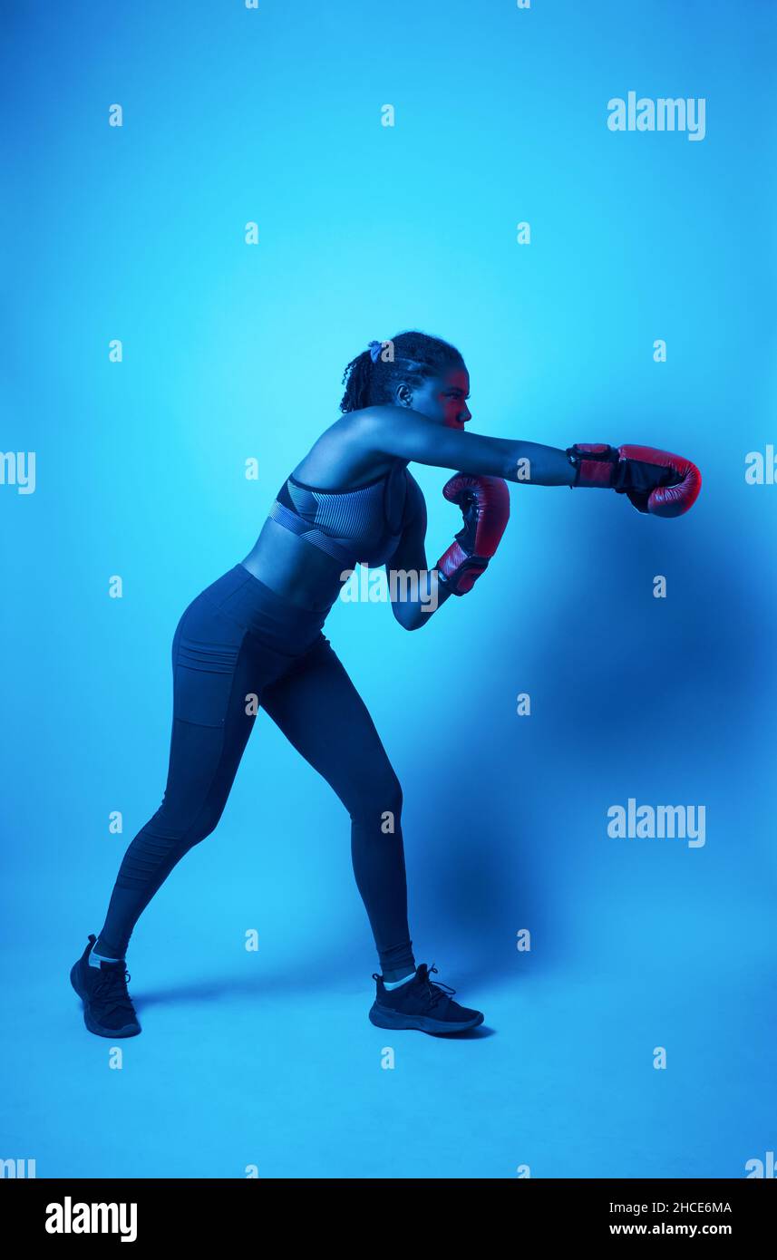 Side view of black female fighter in boxing gloves standing in blue ...