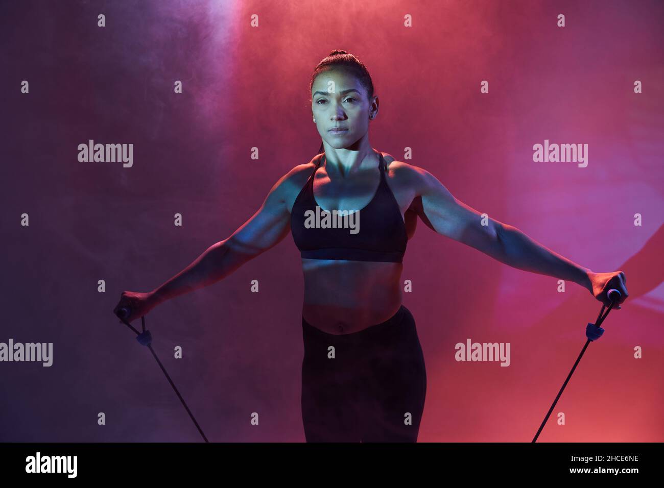 Concentrated strong female athlete in sportswear standing with raised ...