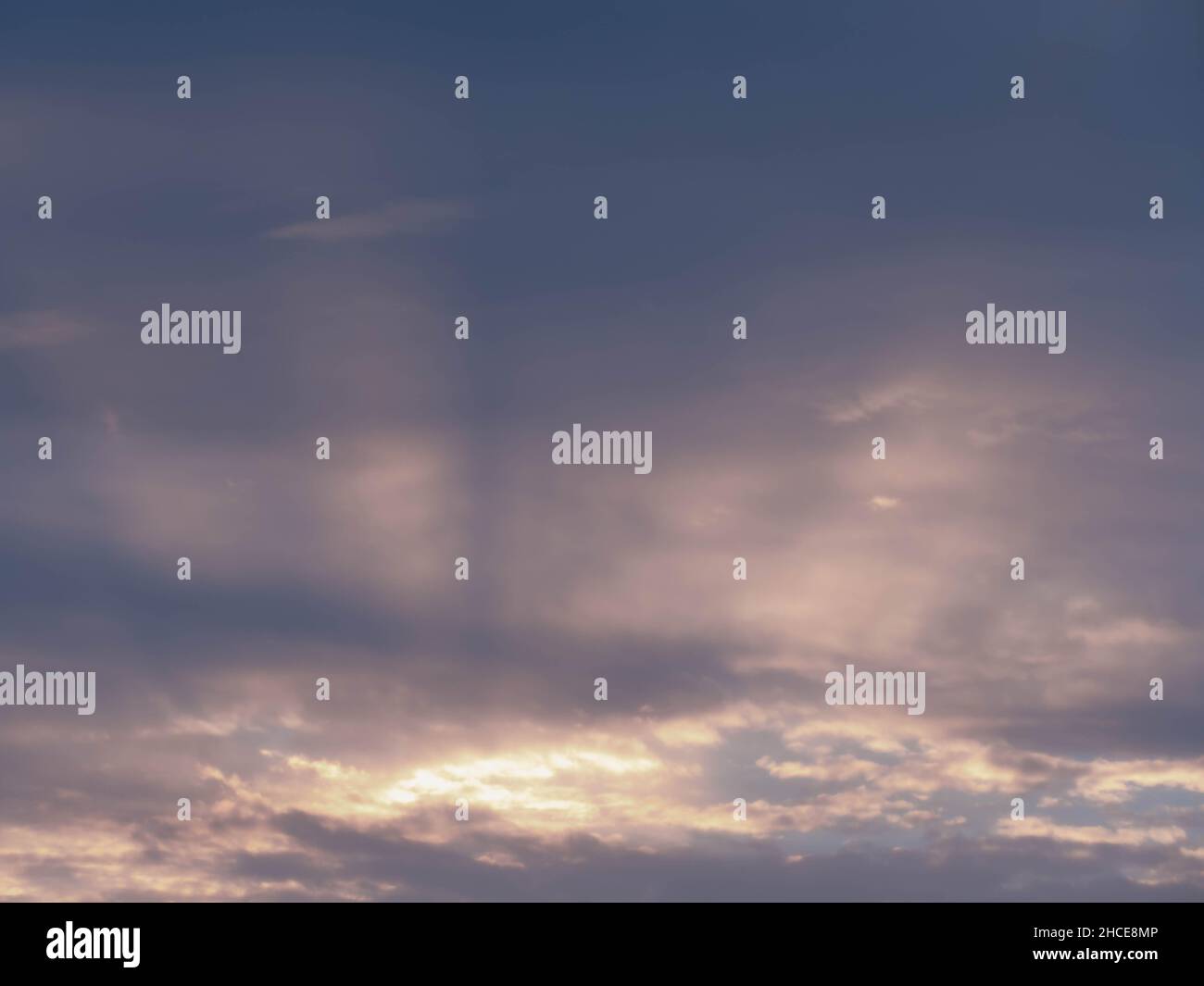 Cloudy sky. Red rays of the setting sun penetrate the crack in the ...