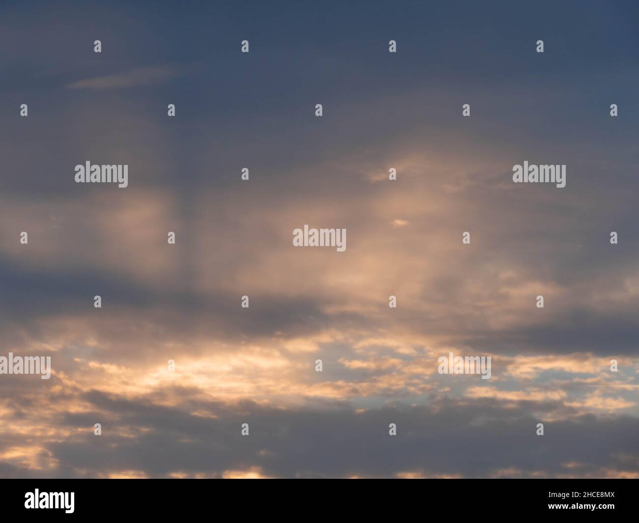 Cloudy sky. Red rays of the setting sun penetrate the crack in the ...