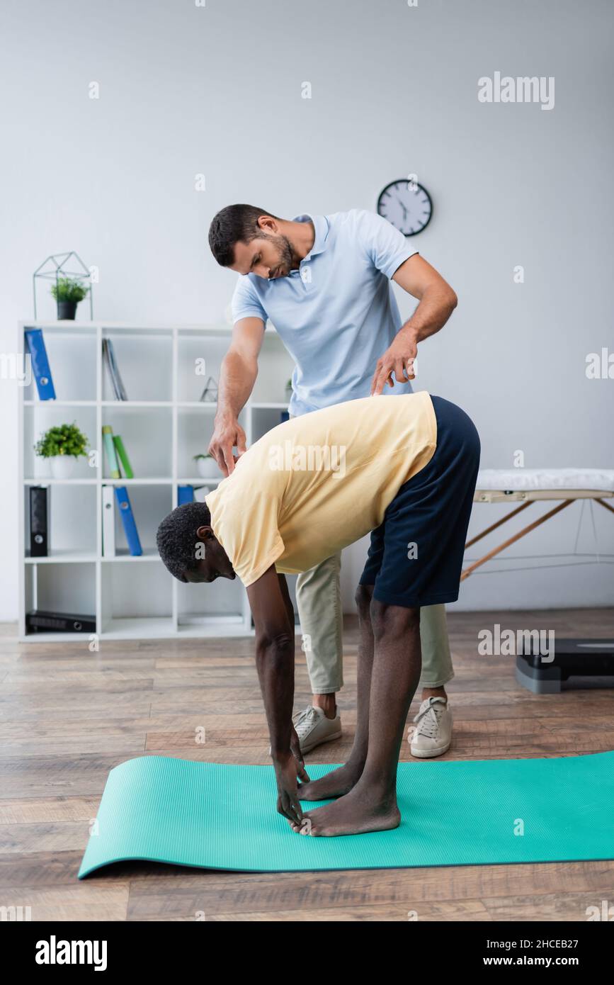 mature african american man doing forward bend exercise near young ...