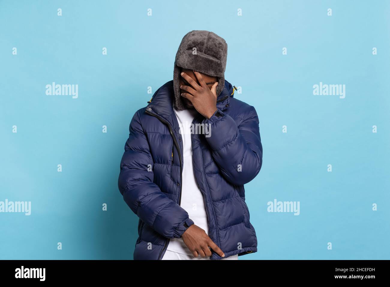 One young sad man, student wearing warm jacket and fur hat posing ...