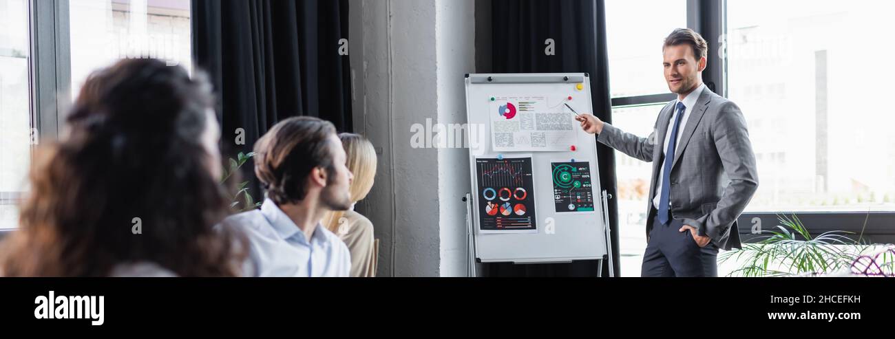 businessman pointing at flip chart with graphs near colleagues on ...