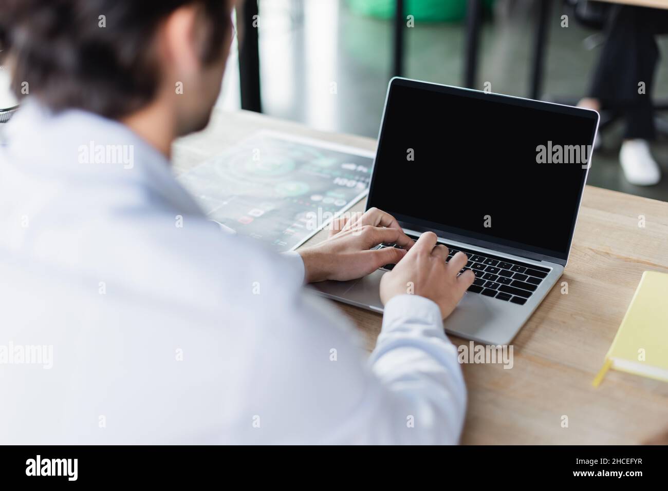 partial view of blurred businessman typing on laptop with blank screen ...