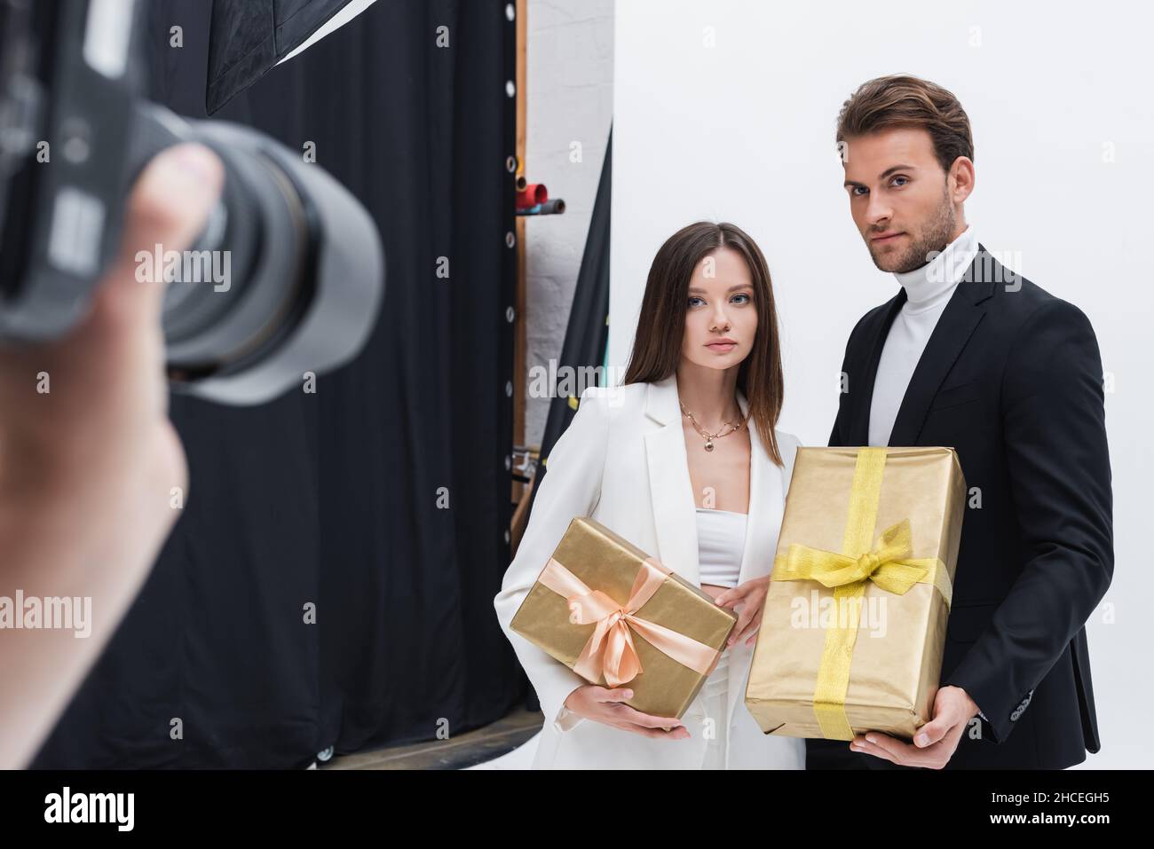 blurred photographer taking photo of models in suits posing with gift ...
