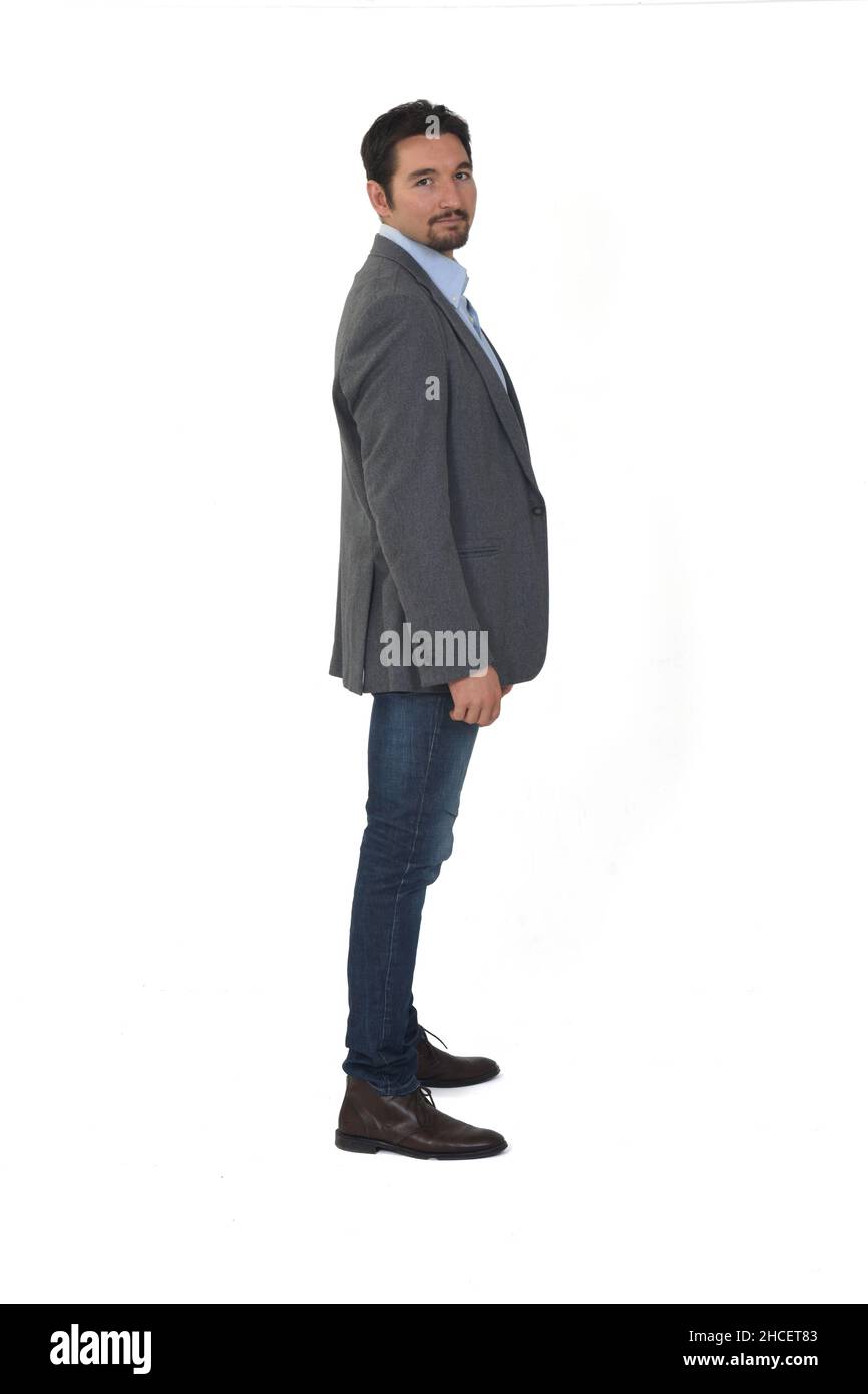 side view of a man with blazer and jeans looking at camera on white ...