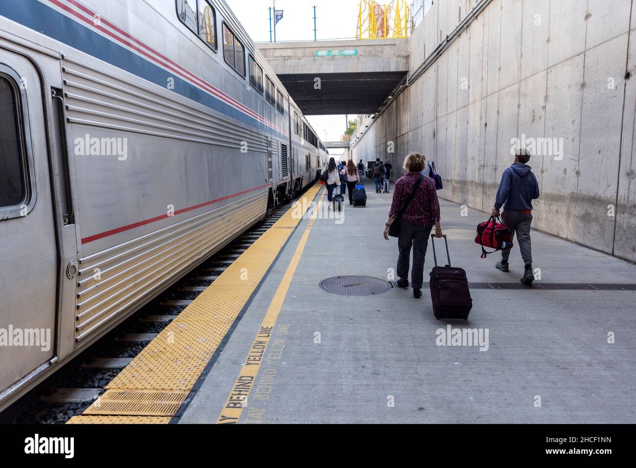 People carrying luggage walk down a platform to board the passenger ...