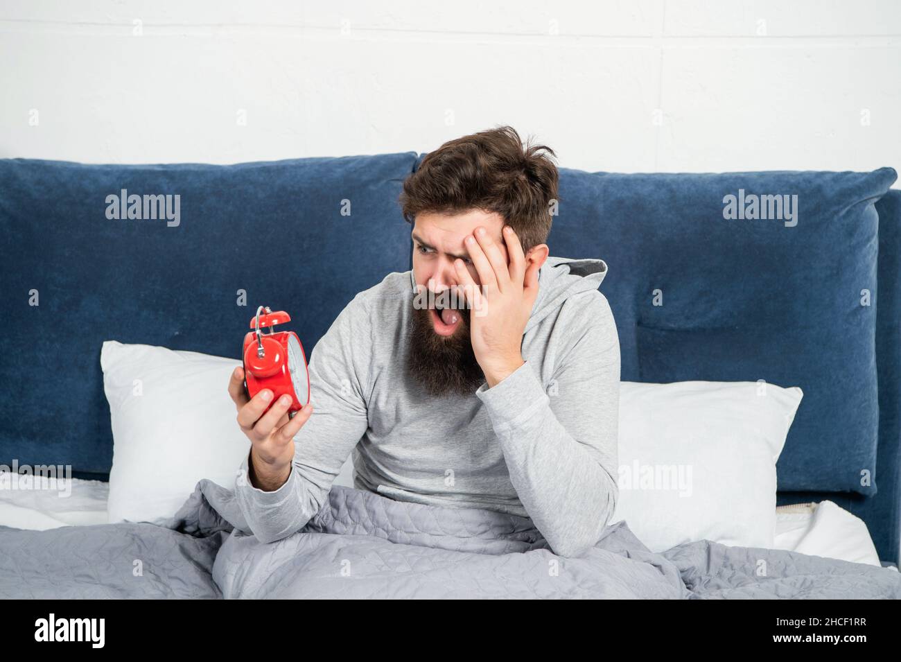 Awaken man screaming in panic looking at alarm clock in bed in morning ...