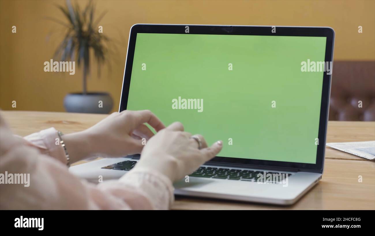 Over the shoulder view of a woman hands using laptop with green screen ...