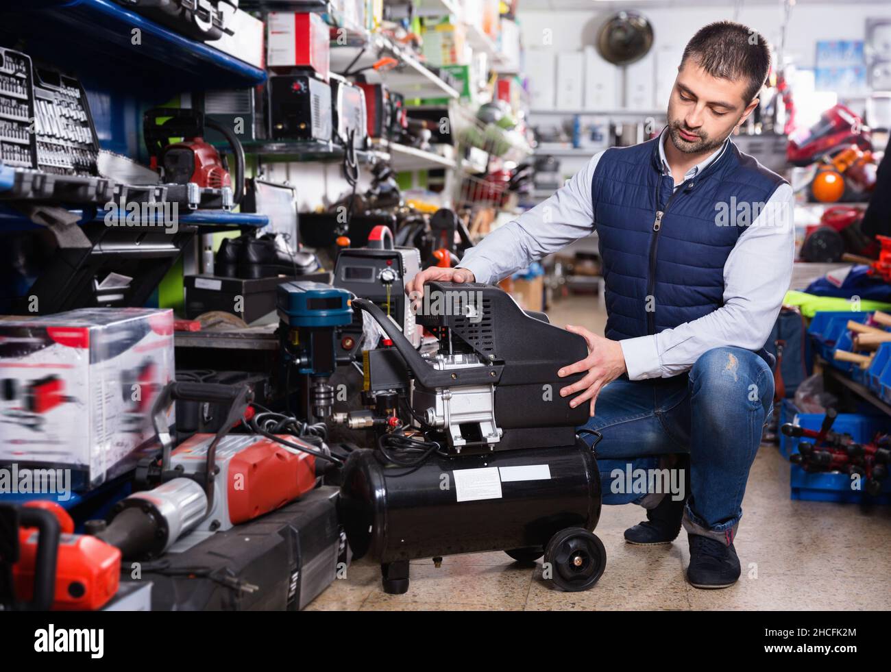 Adult male is standing with air compressor in tools store Stock Photo ...