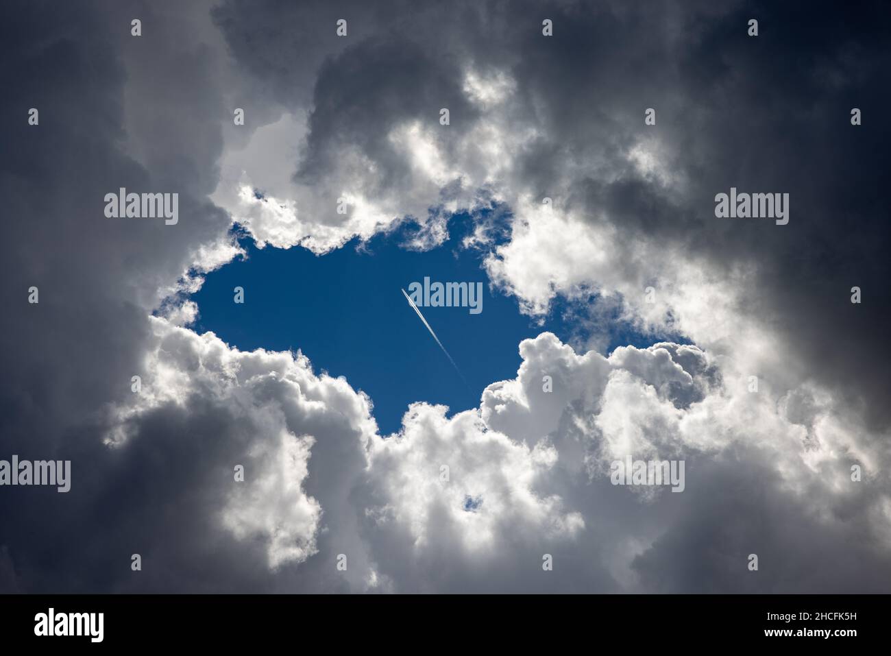 Low angle shot of an airplane stream surrounded by clouds in a blue sky ...