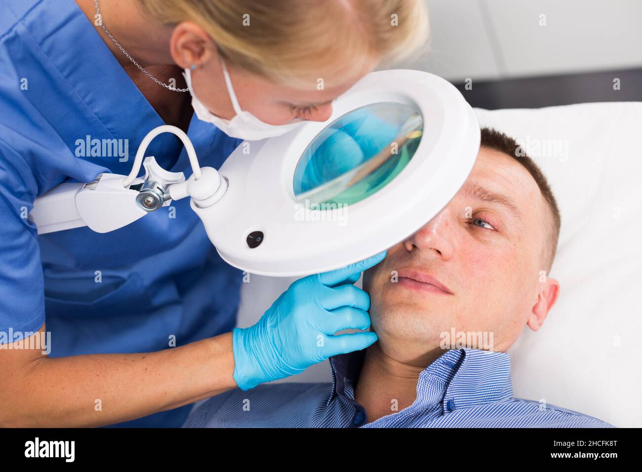 Woman specialist is cleaning skin of patient with using magnification ...