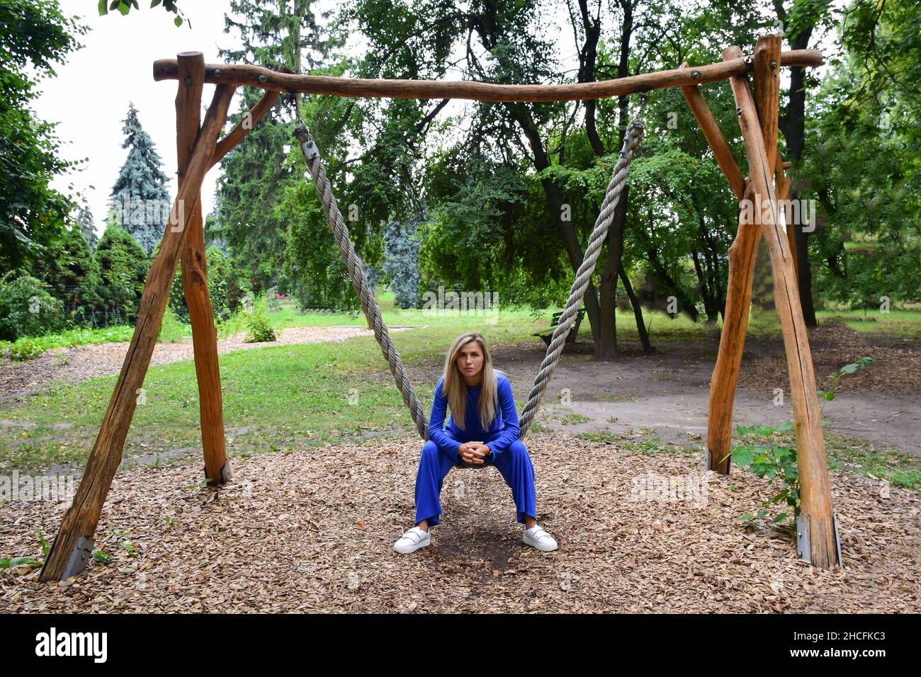 Attractive blonde woman sitting on a hanging rope swing from a tree in ...