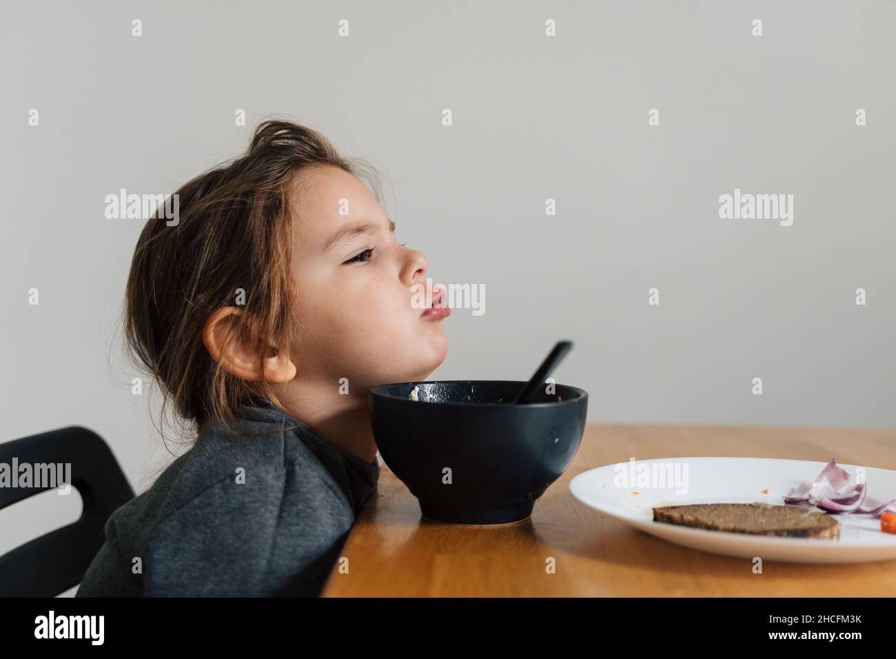 Unhappy child girl eats soup from black bowl with bread and onion ...