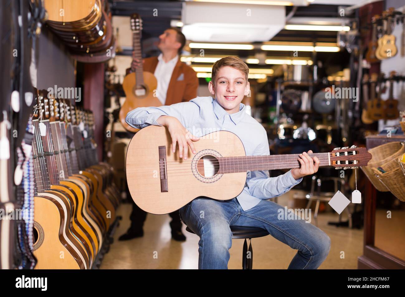 Happy seller showing guitar to boy client Stock Photo - Alamy