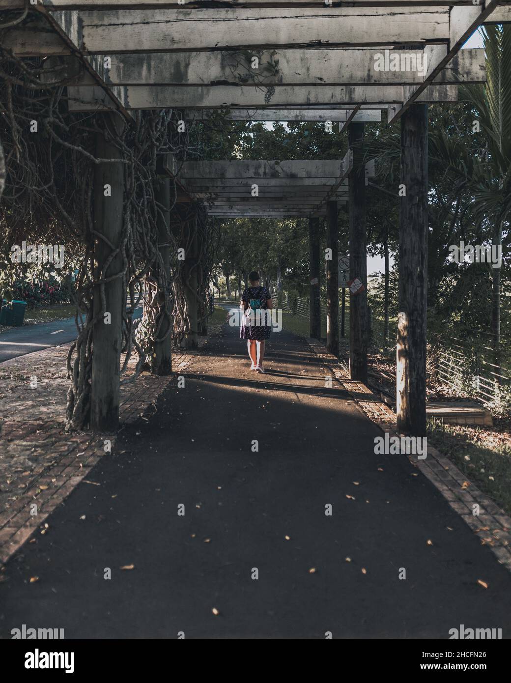 Vertical back view of a female walking underneath a wooden structure in ...