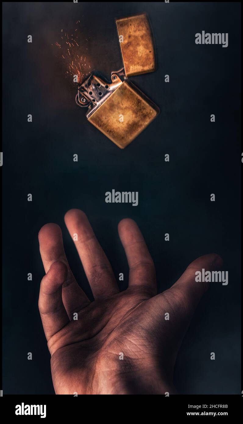 Vertical shot of a man's hand throwing up a metallic lighter while ...