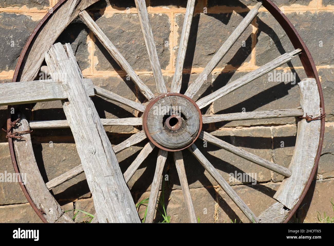 Vintage wooden cartwheel with a metal rim leaning against a stone wall ...