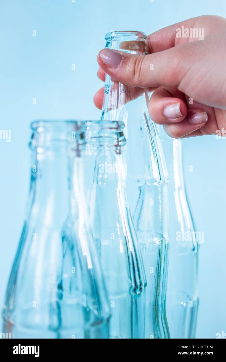 Caucasian hand taking a glass bottle with a bright blue background ...