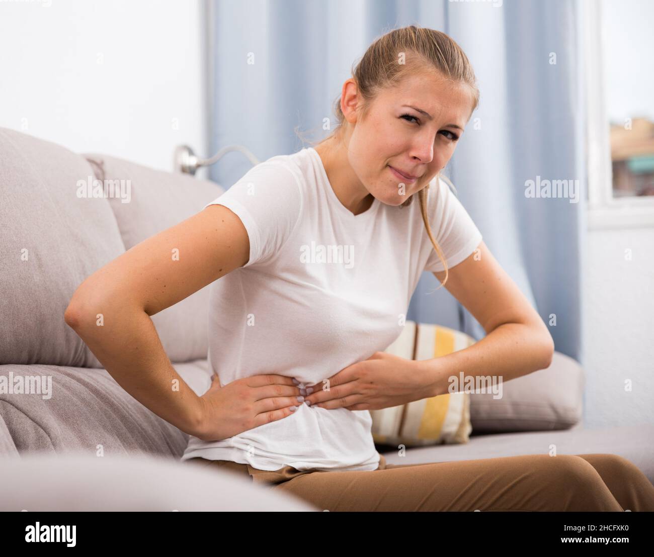 Girl is sitting unhappy because she has a stomach ache Stock Photo - Alamy