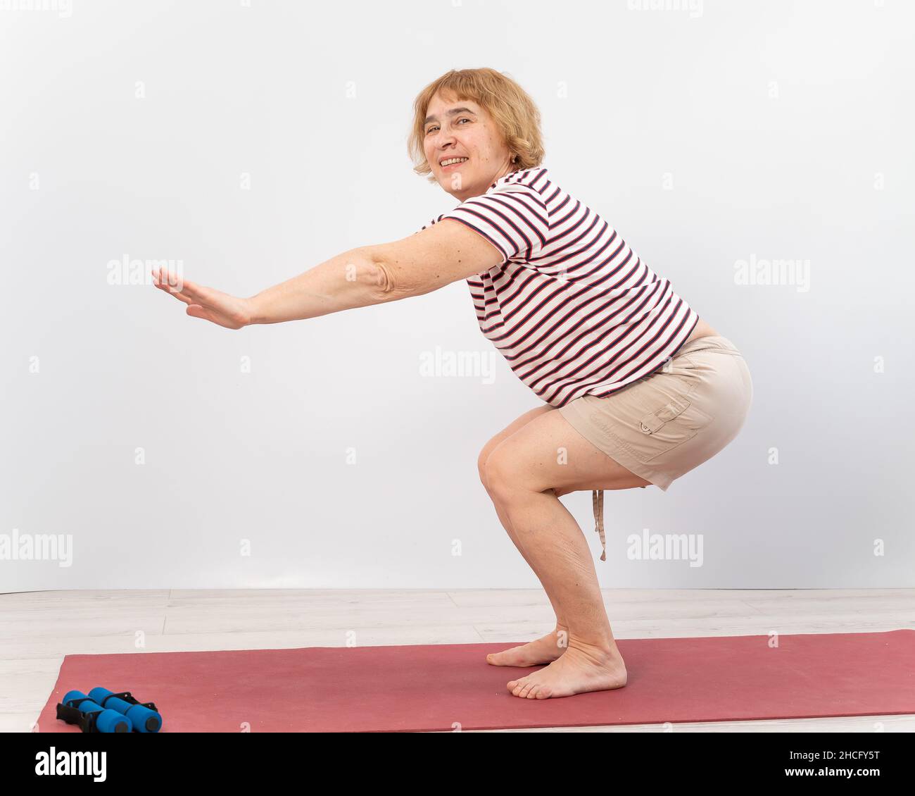 Elderly woman doing squats on a white background. The old lady is doing ...