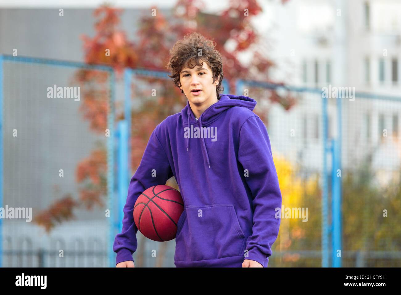 Cute teenager in violet hoodie playing basketball. Young boy with ball ...
