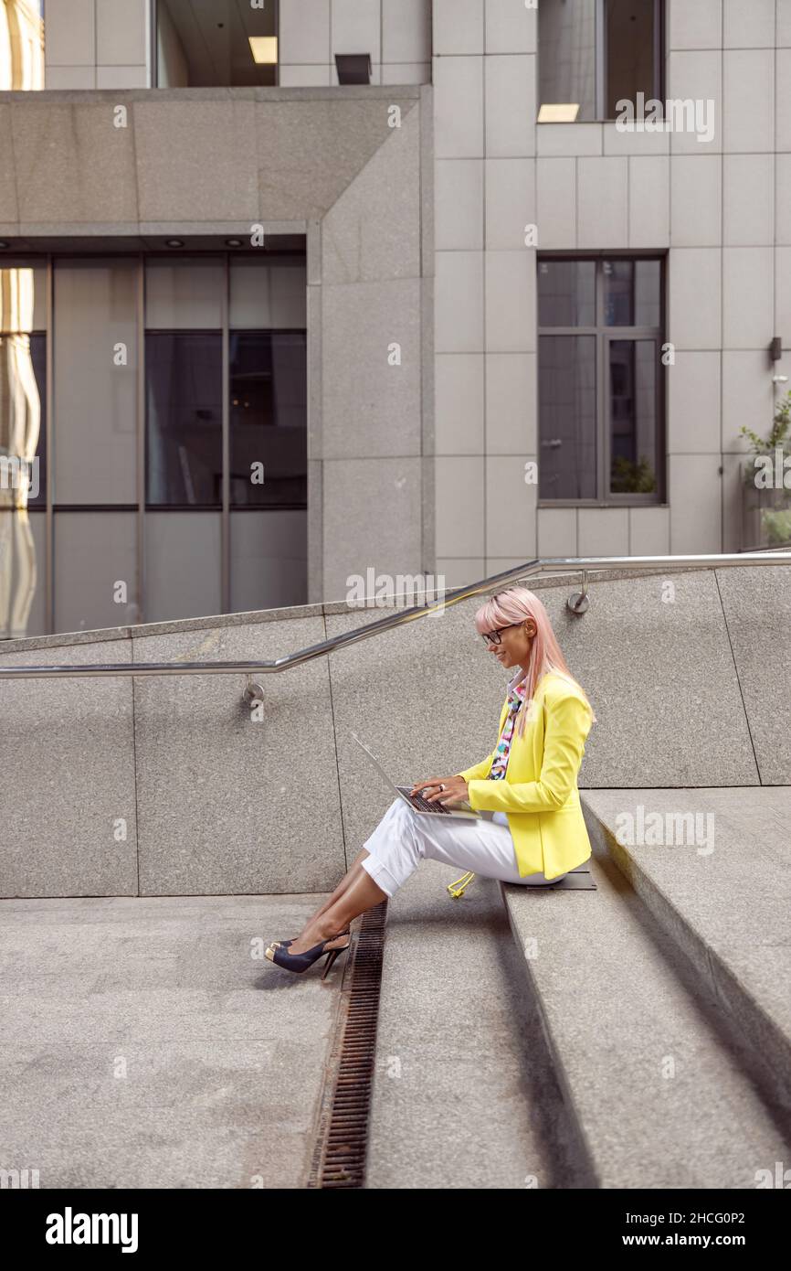 Female smiling while typing on laptop on street stairs Stock Photo - Alamy