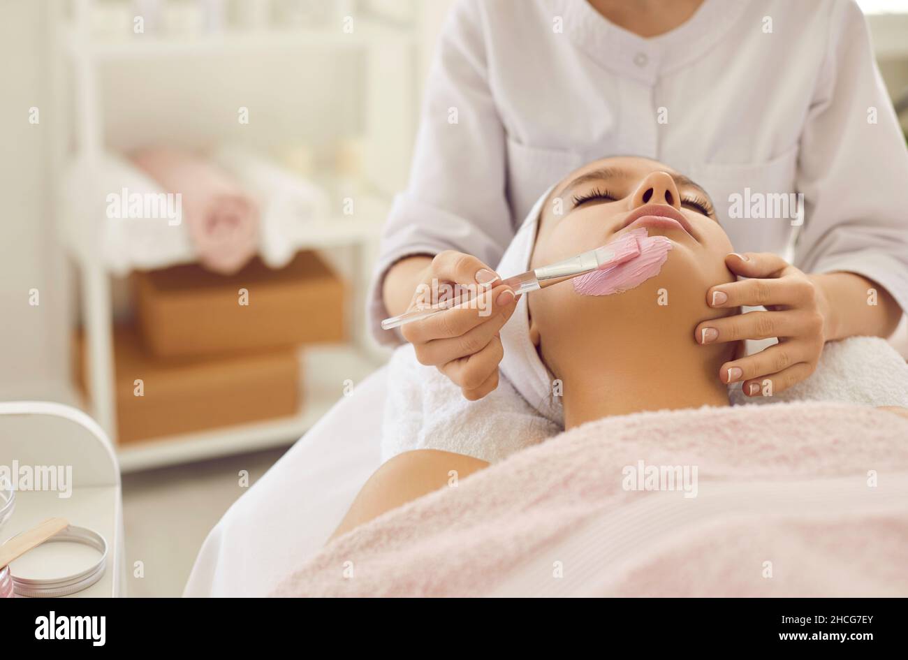 Woman getting facial mask procedure done by skin professional in spa or ...