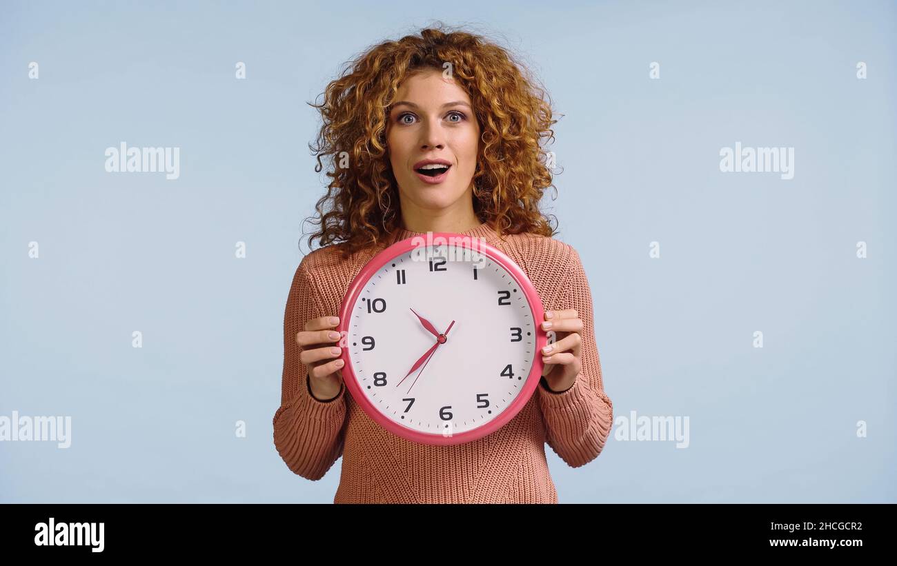 amazed redhead woman with open mouth holding round clock isolated on ...