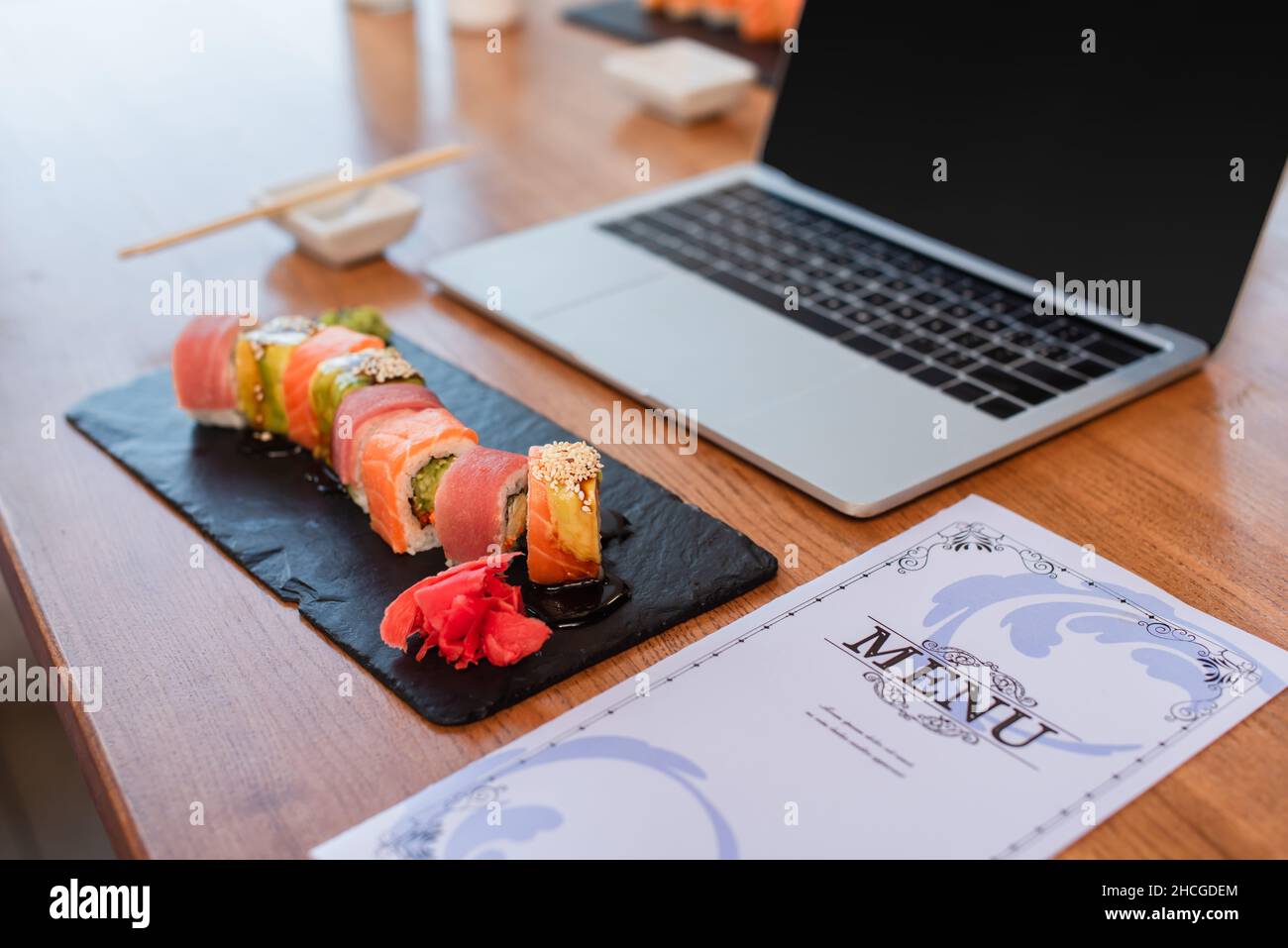 delicious sushi rolls, menu and blurred laptop with blank screen on ...