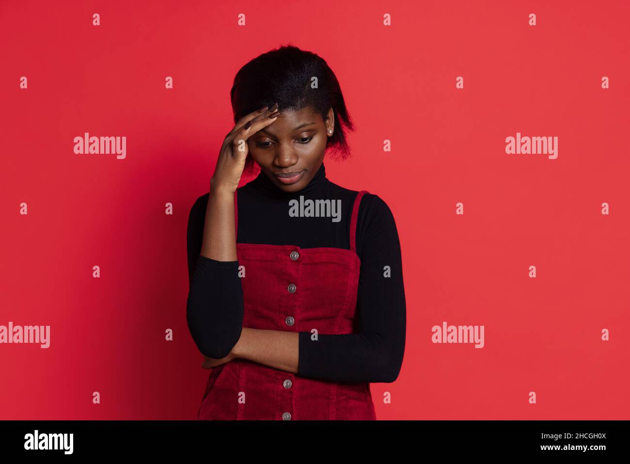 Sad young dark skinned girl isolated on dark red studio background ...
