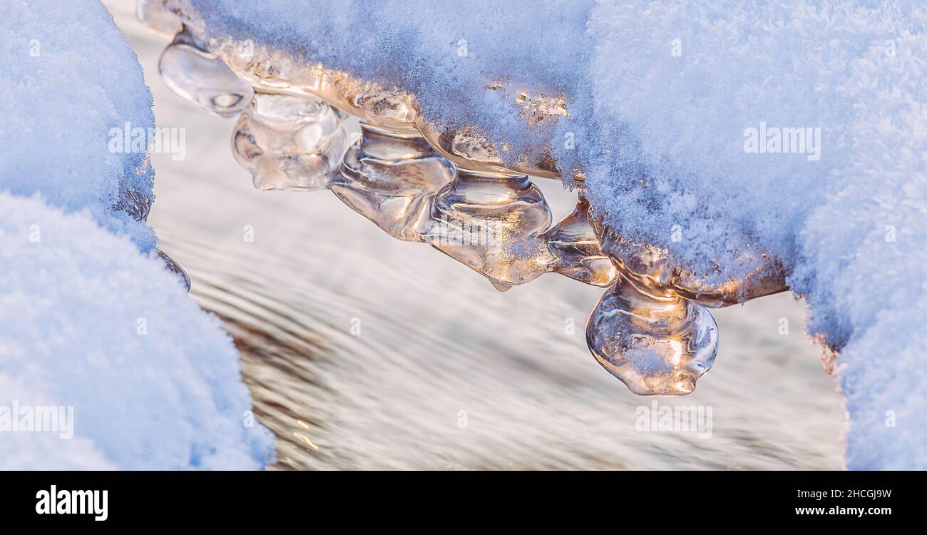 Tree branches with icicles over the water in the river. Natural ...