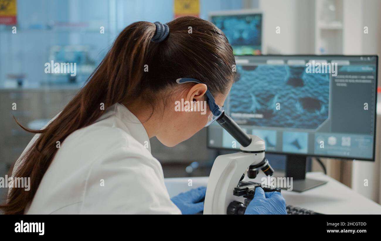 Woman examining dna sample on microscope tray in laboratory to analyze ...