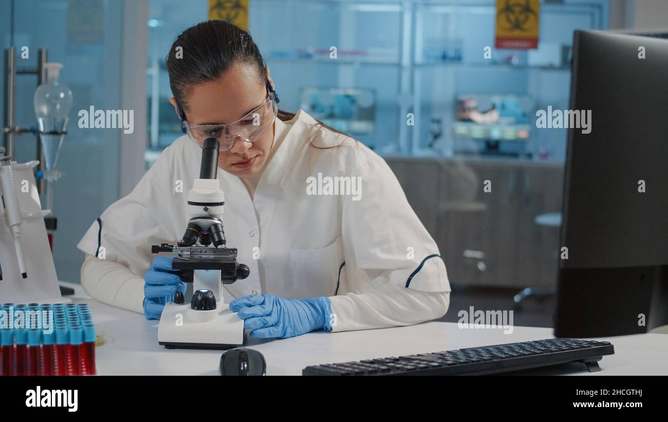 Specialist with safety goggles using microscope in laboratory, working ...