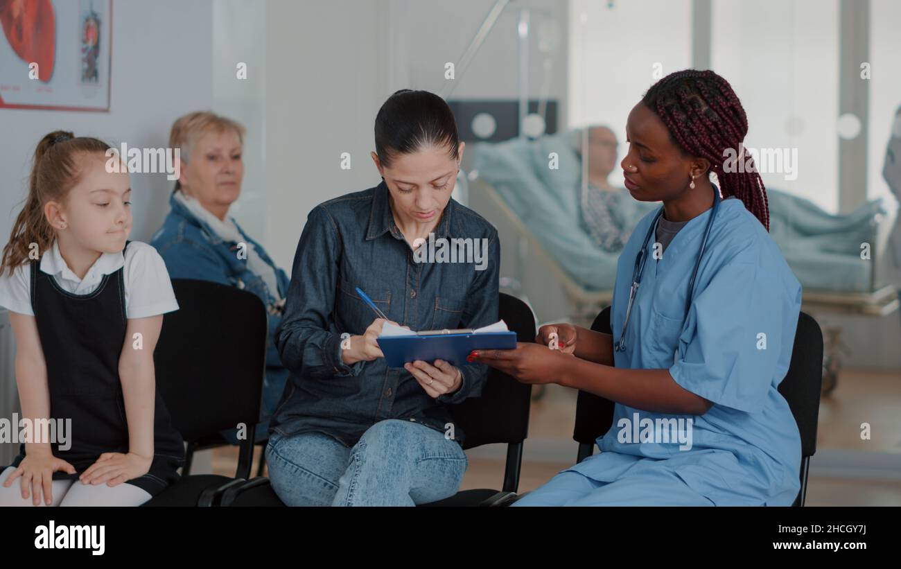 Mother with child signing checkup papers in waiting room, talking to ...