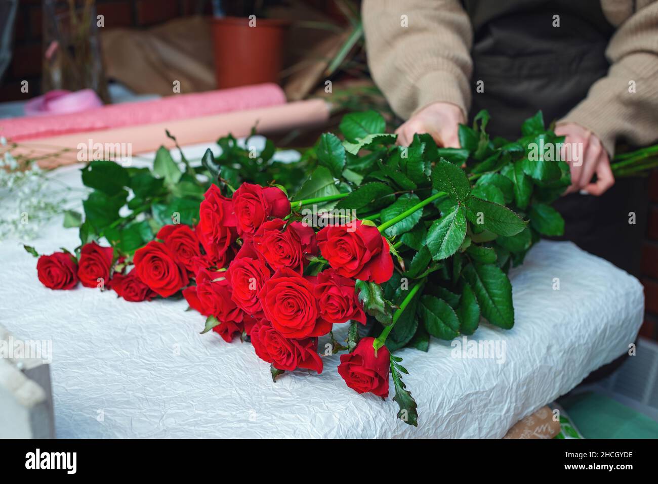 Female florist create a bouquet of fresh red roses at workplace. Floral ...