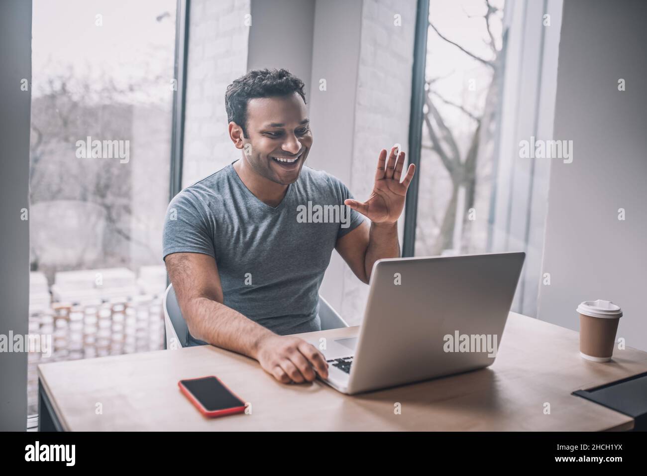 Guy gesturing greeting in front of laptop screen Stock Photo - Alamy