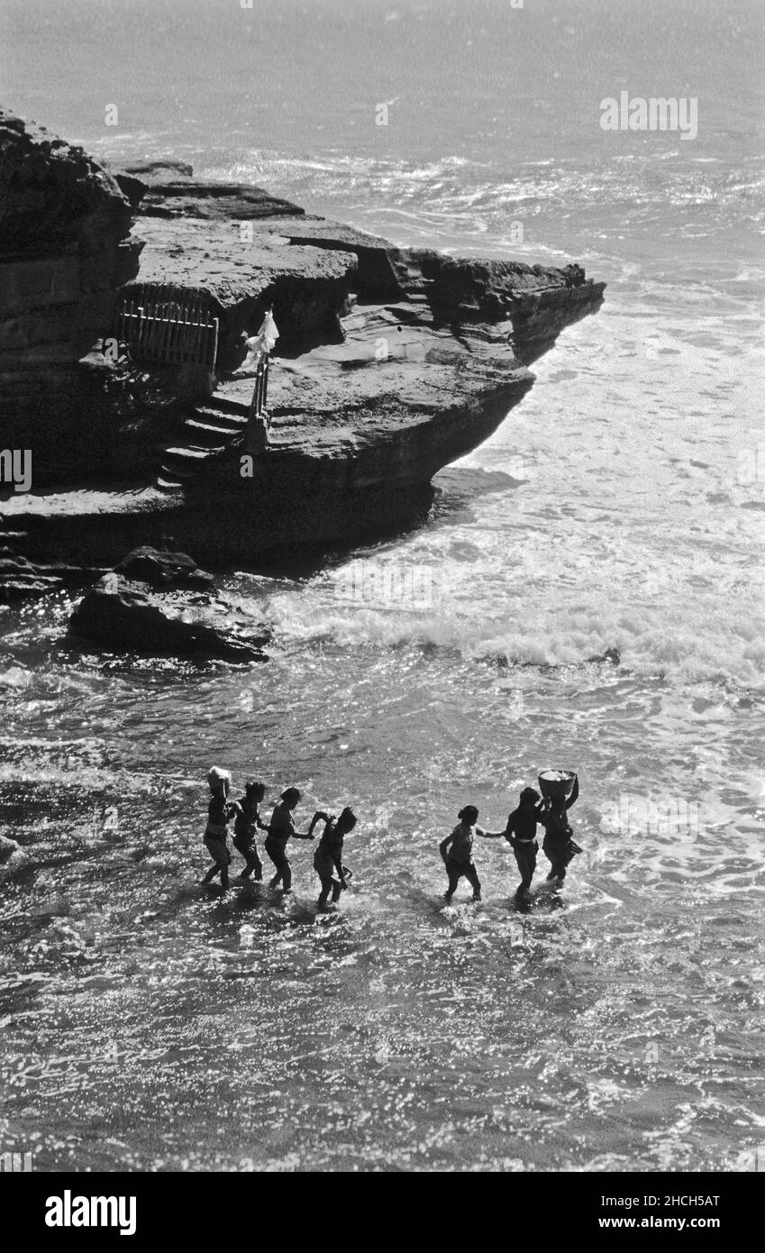 Women helping each other wade from temple to rock through the current ...