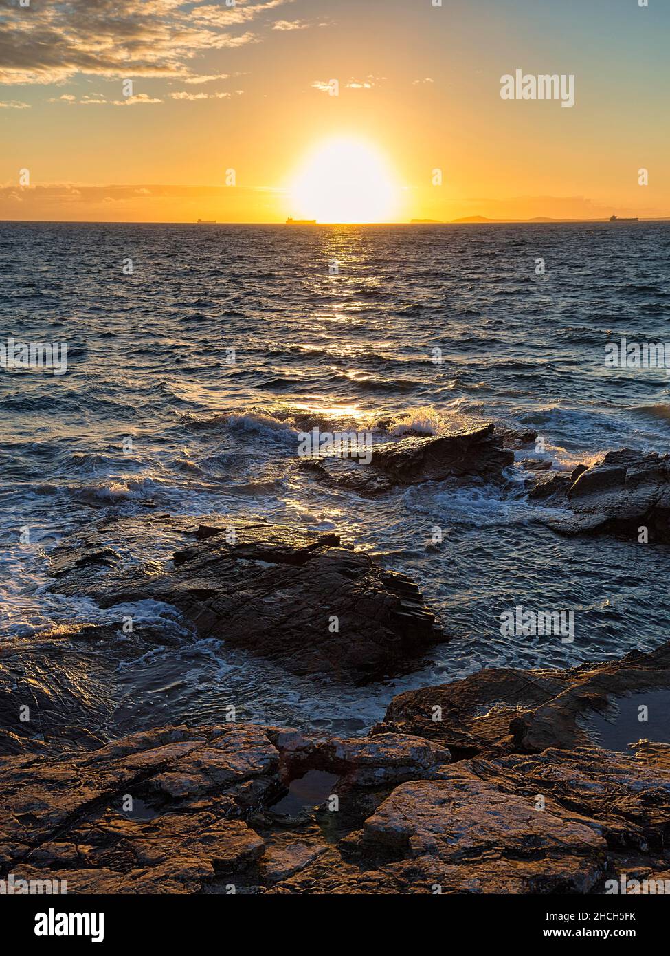 Sunset by the sea, rocky coast, container ships on the horizon ...