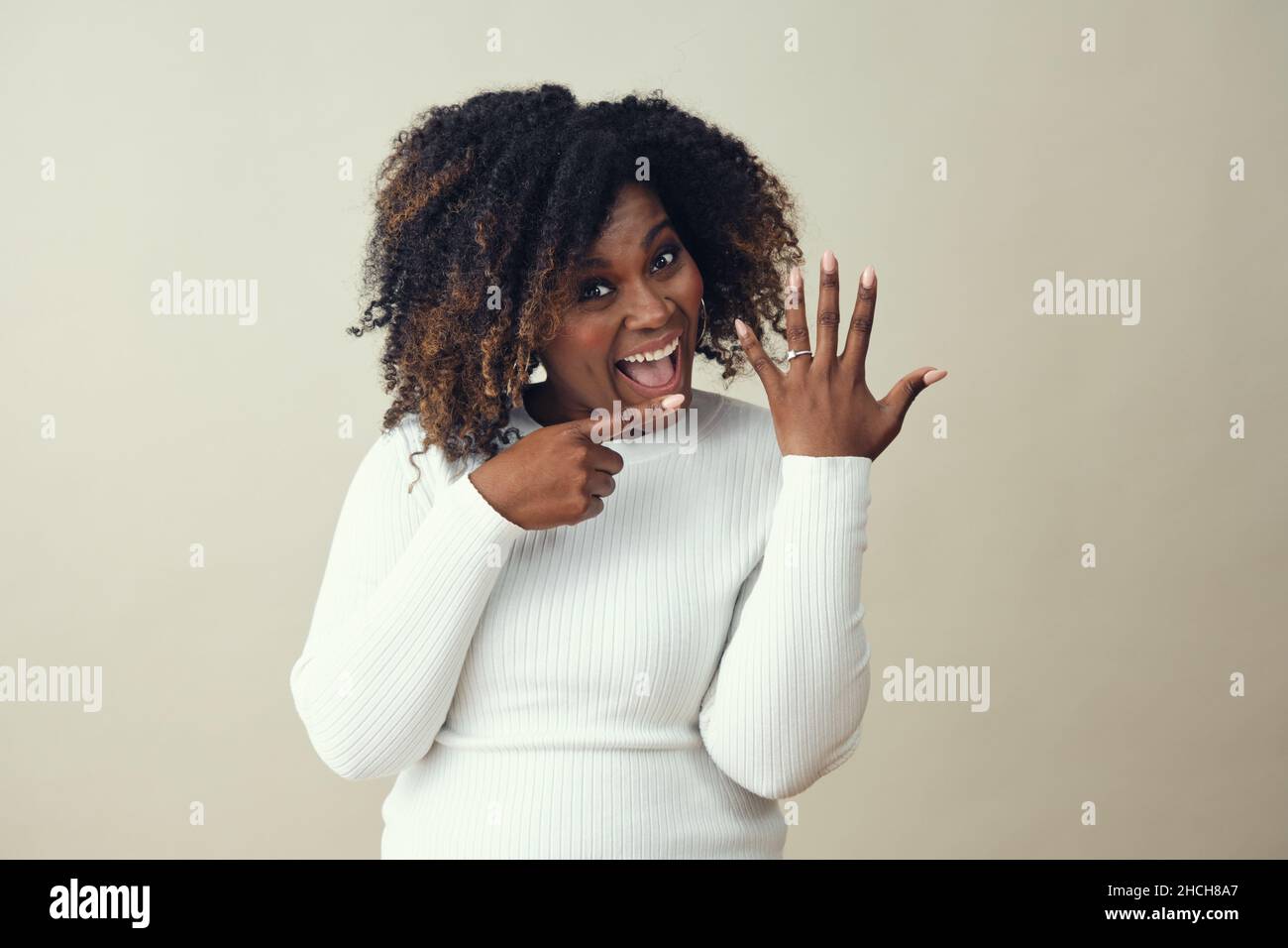 Portrait of ecstatic woman pointing at engagement ring against white ...