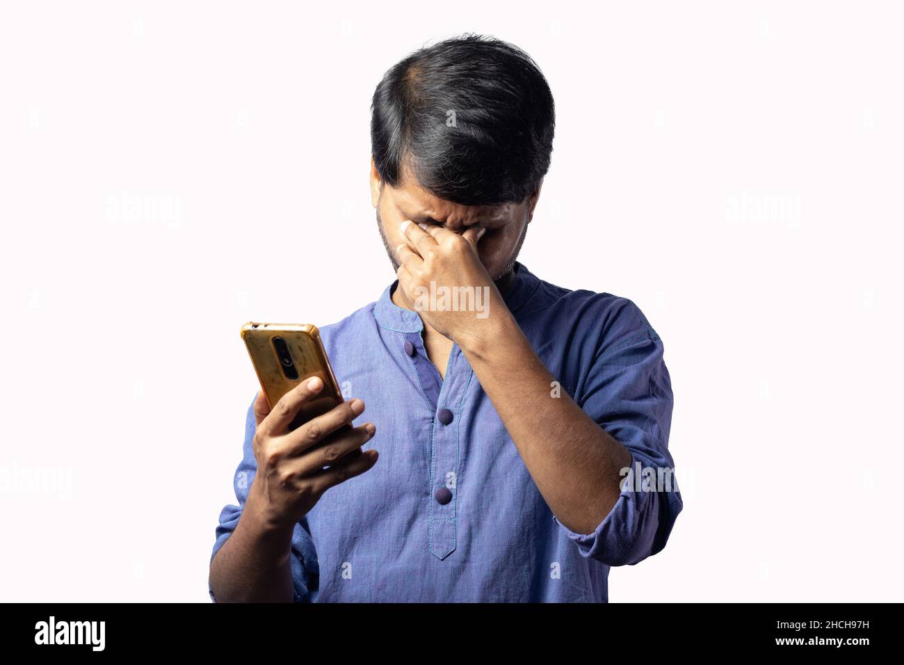 A young Indian male in blue dress facing eyes problem using smart phone ...
