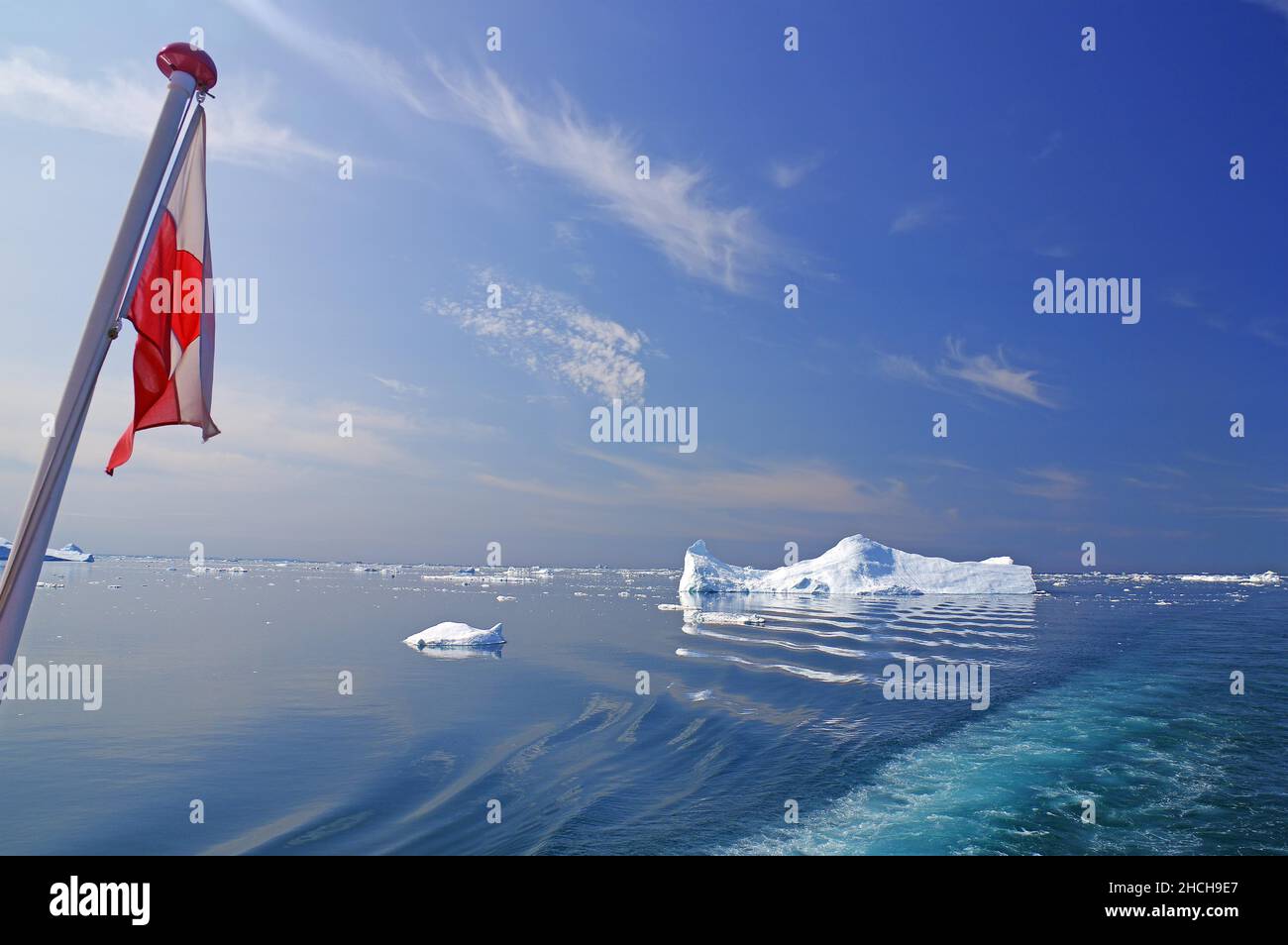 Greenlandic flag and icebergs in the calm waters of Disko Bay ...