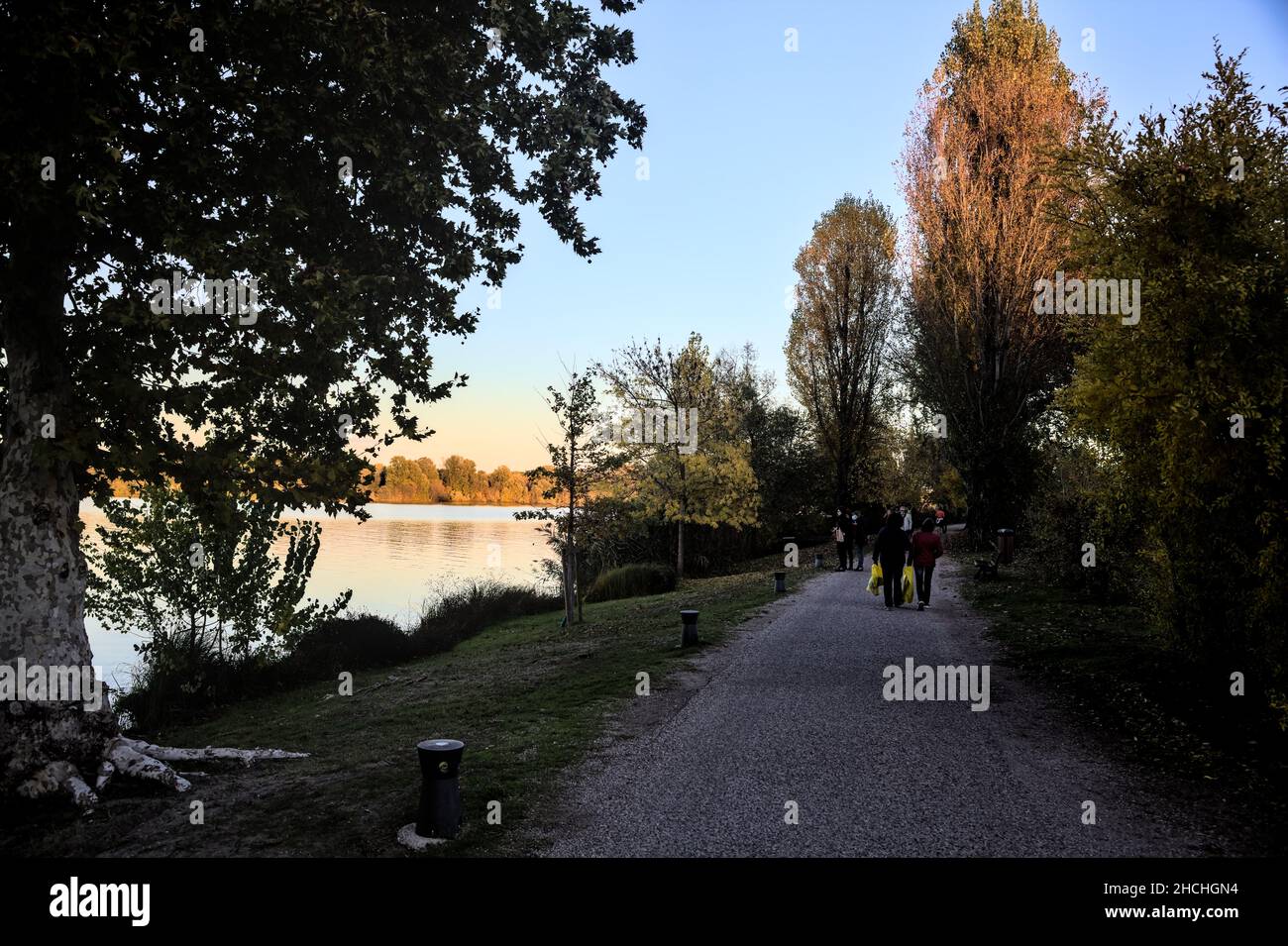 Gravel path by the riverside in a park at sunset in autumn with people ...