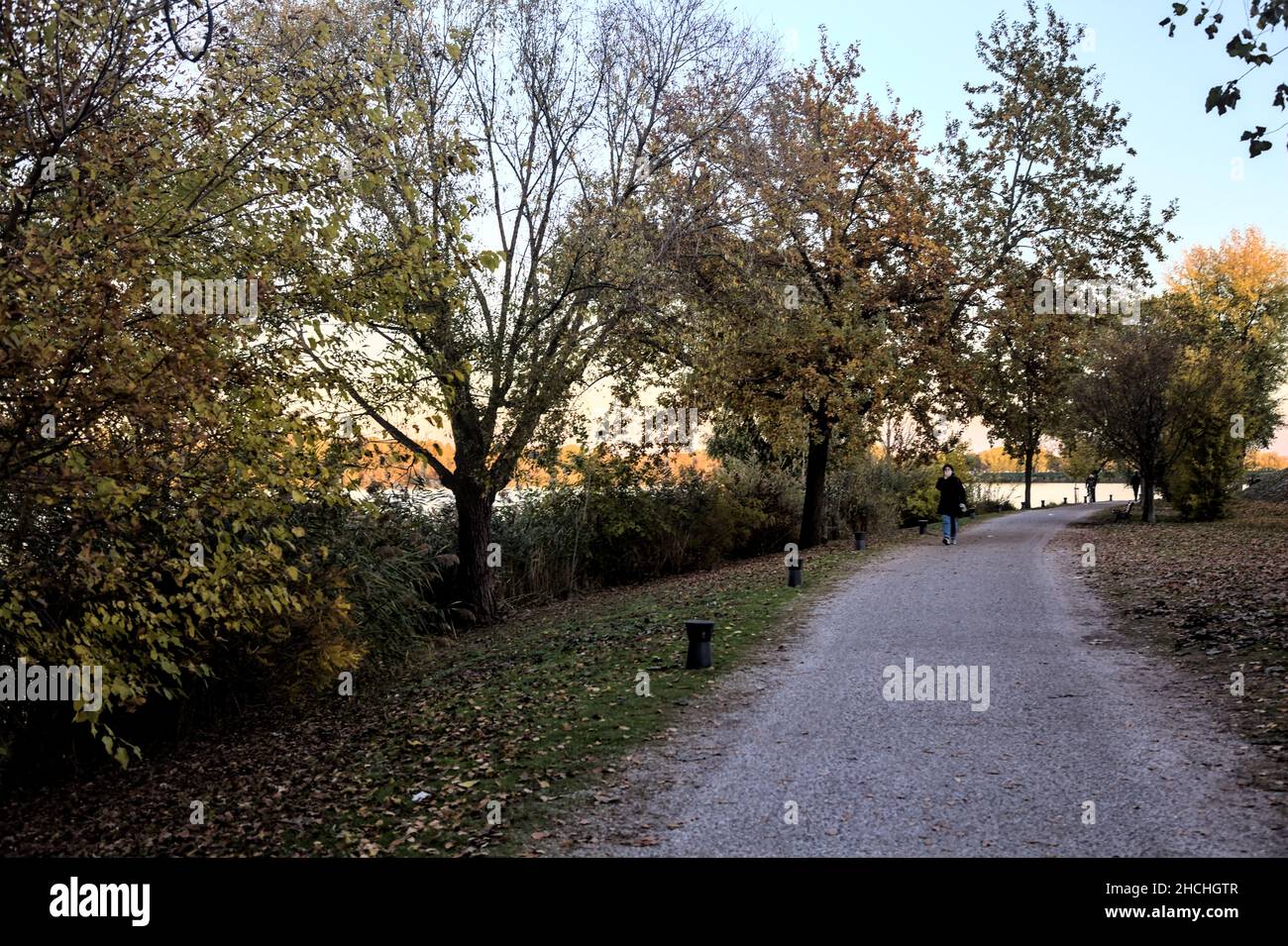 Gravel path by the riverside in a park at sunset in autumn with people ...