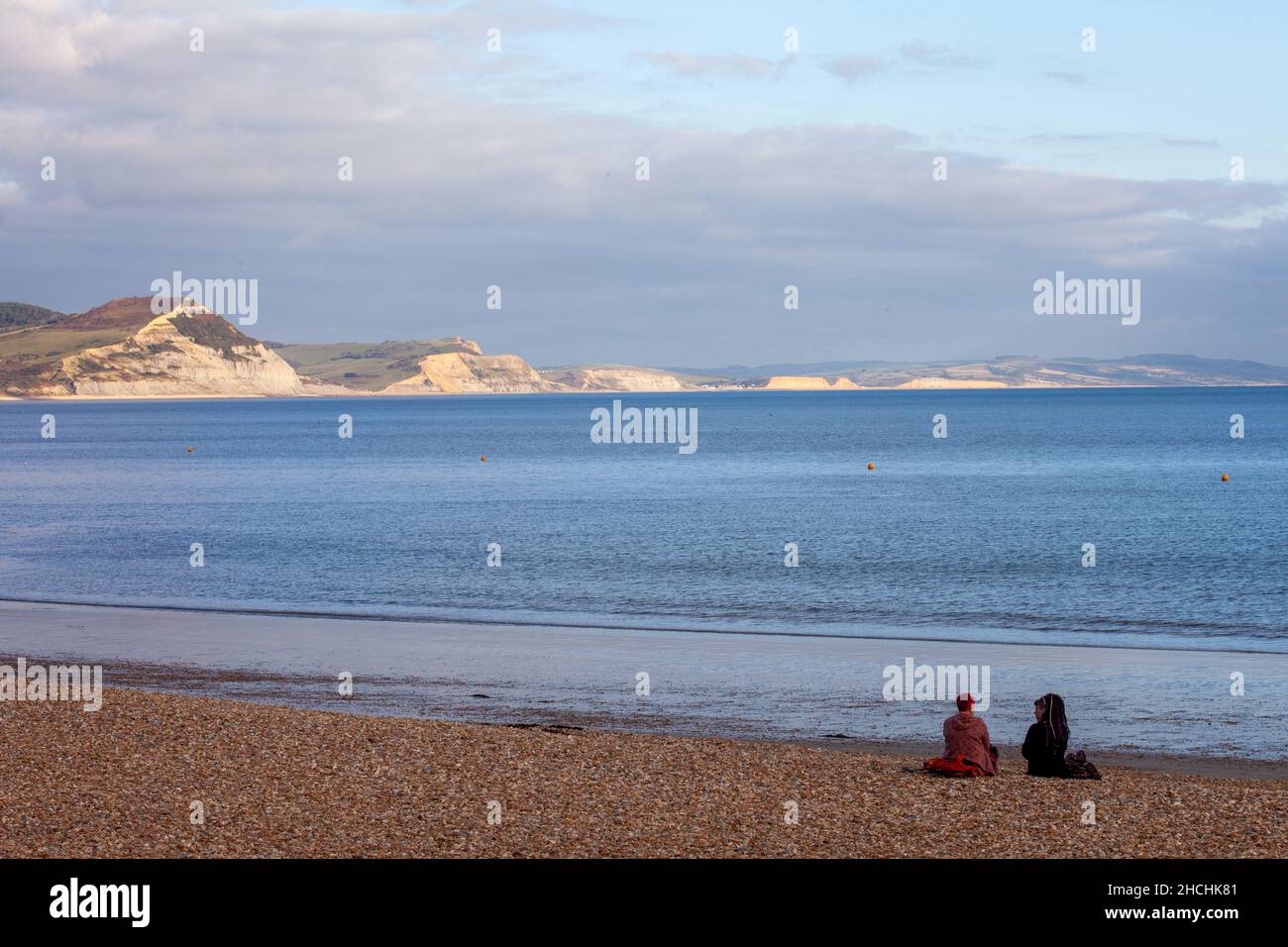 Two peaople sitting on Lyme Regis beach looking across Lyme Bay towards ...